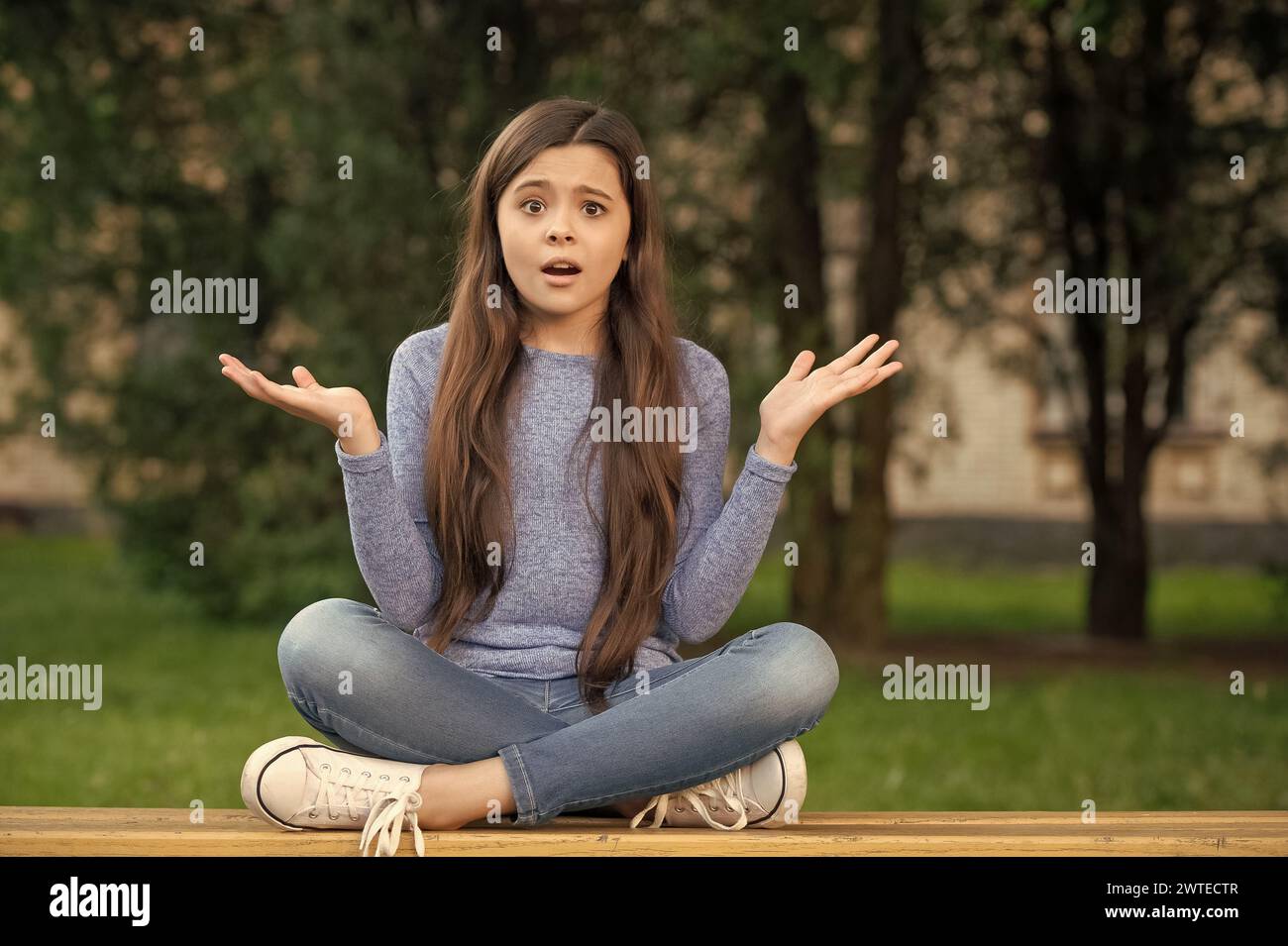 Shocked teenage girl shrugging shoulders sitting legs crossed on bench ...