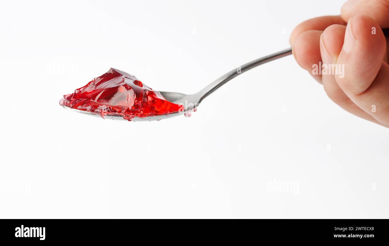 Hand holding a spoon full of red jelly candy isolated on white ...