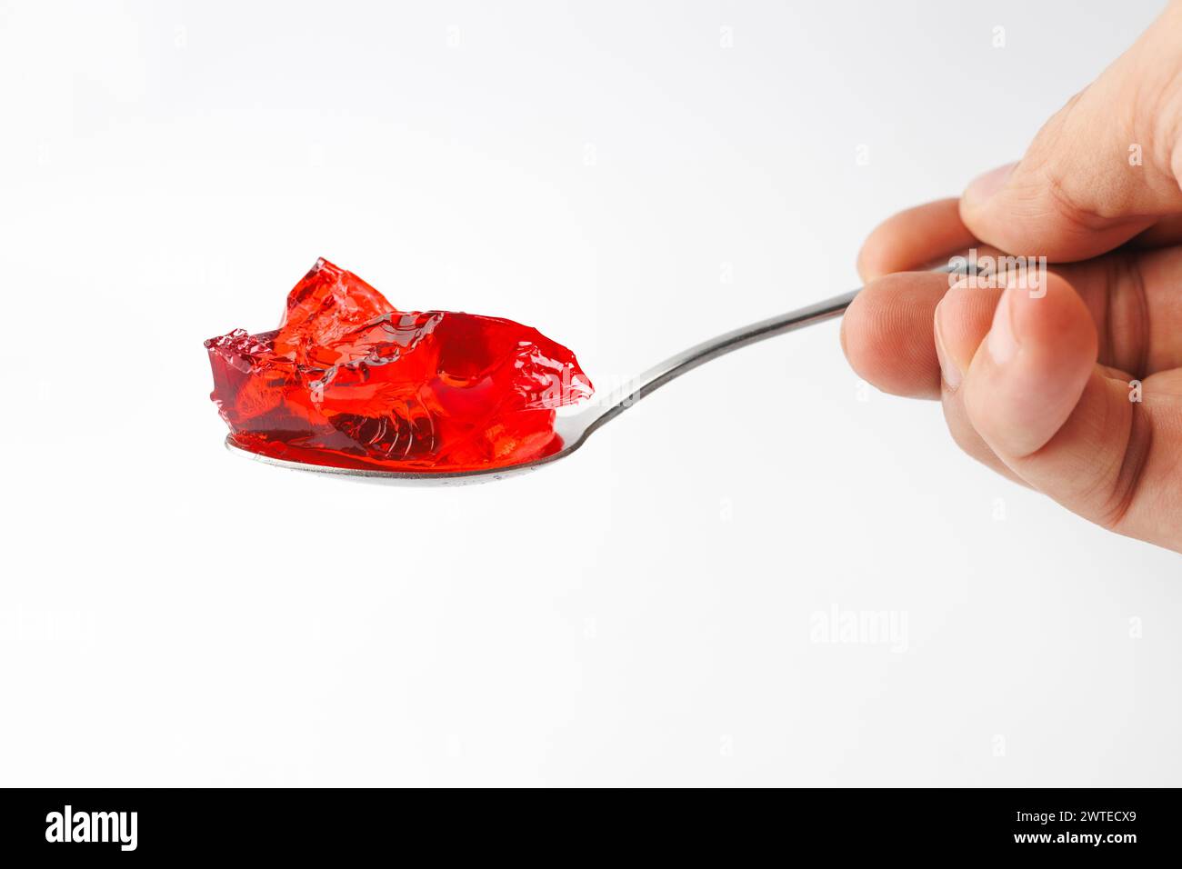 Hand holding a spoon full of red jelly candy isolated on white ...