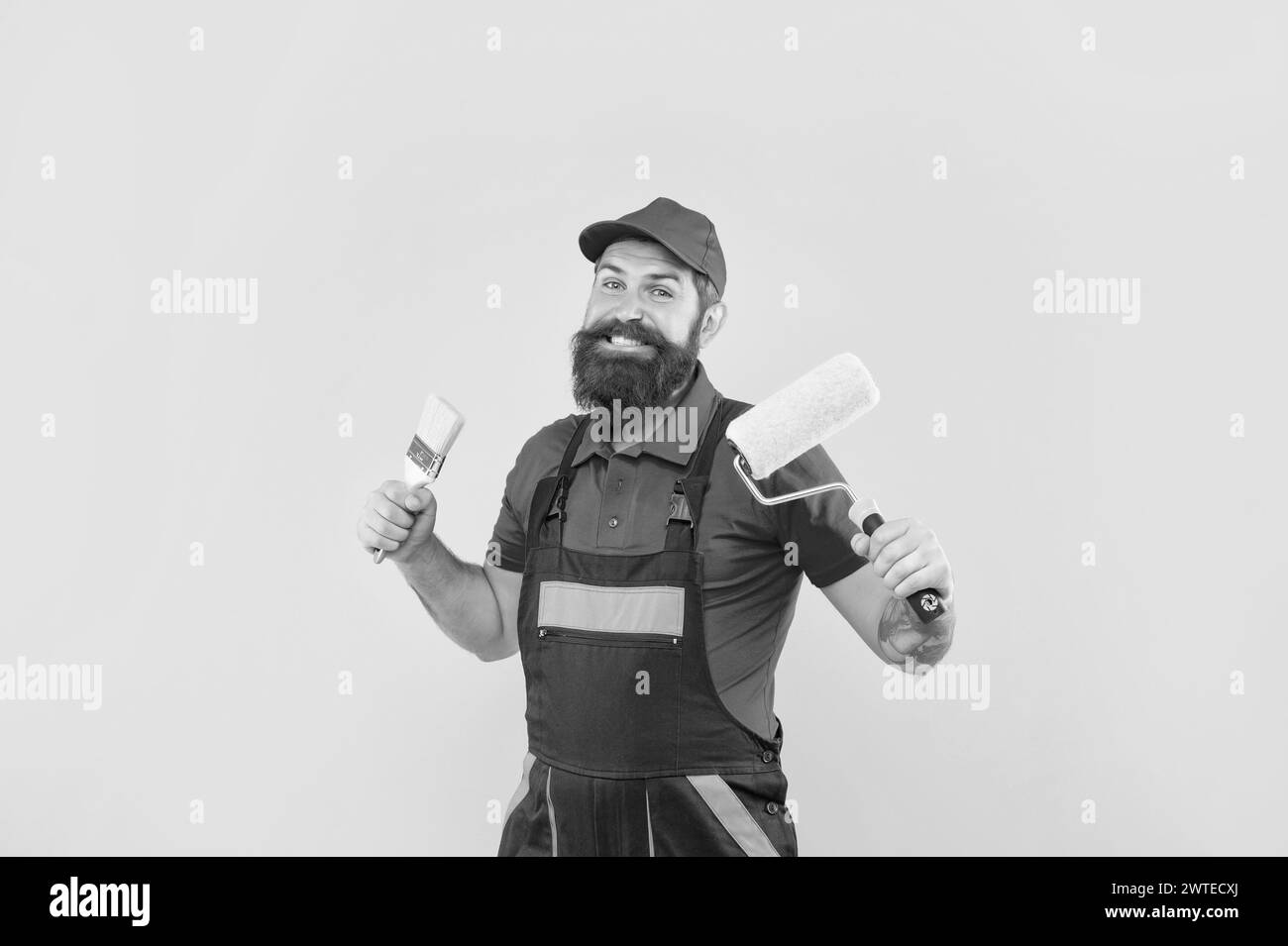 happy bearded man painter in work clothes hold paint roller and brush ...