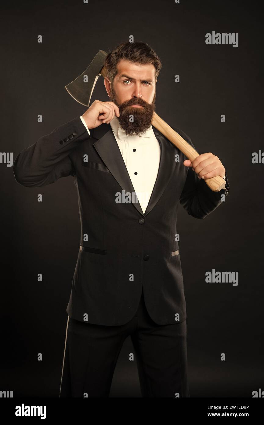Serious bearded man twirling mustache while carrying axe at dark background, barber Stock Photo ...