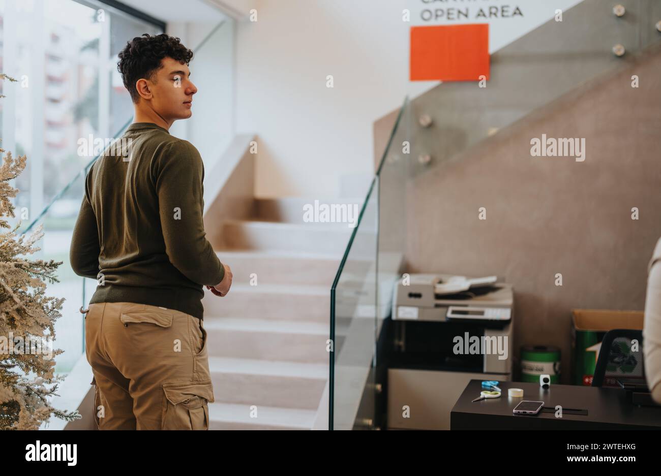 Young man in casual attire standing by reception desk in modern office ...