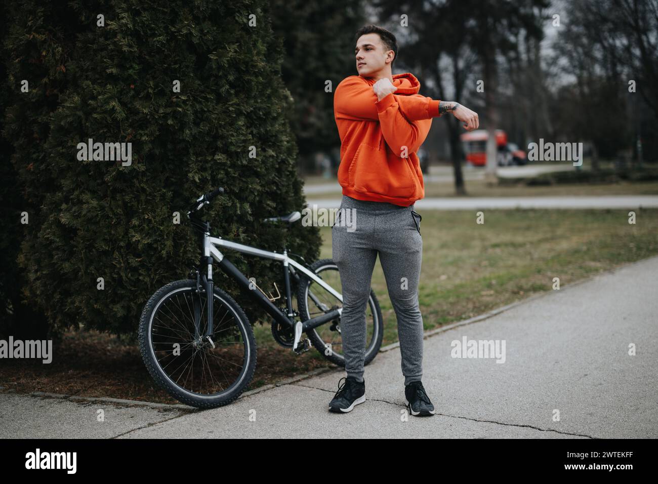 Active young man pausing during a bike ride in the park on a cloudy day ...
