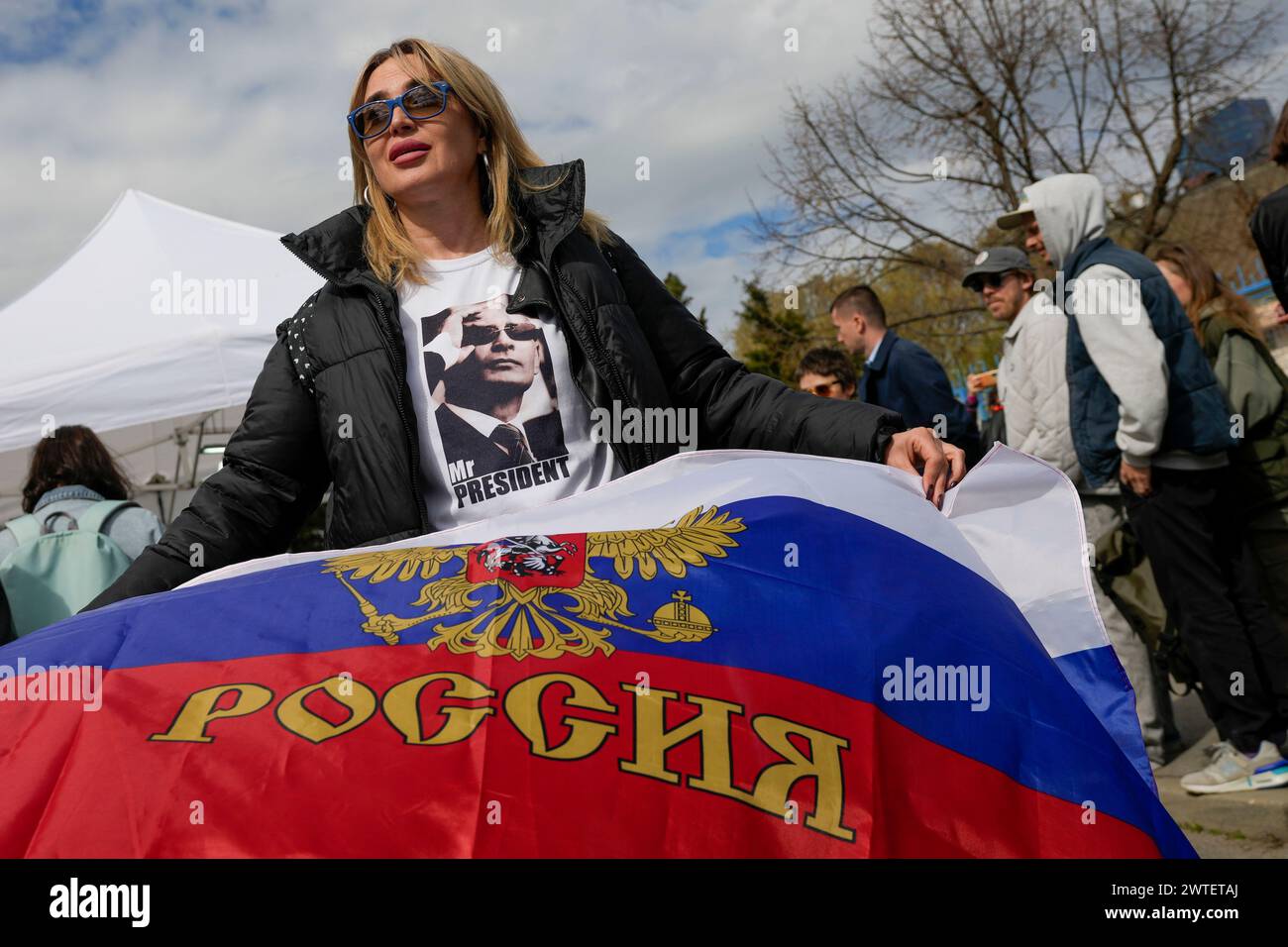 A woman wearing a shirt with a picture of Russian President Vladimir Putin holds a Russian flag ...