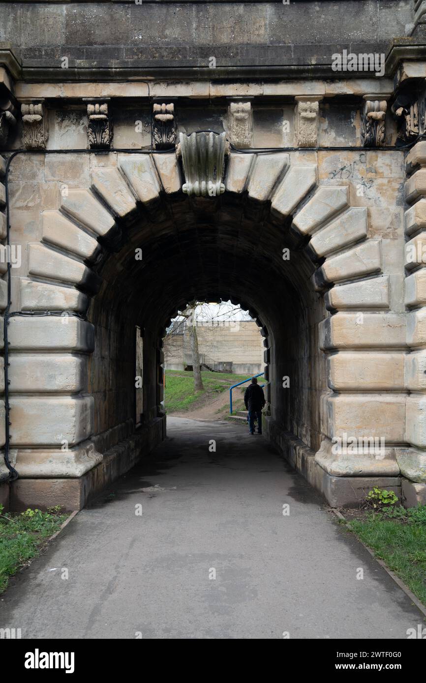 Person walks under a historic stone arch in a serene park setting Stock ...