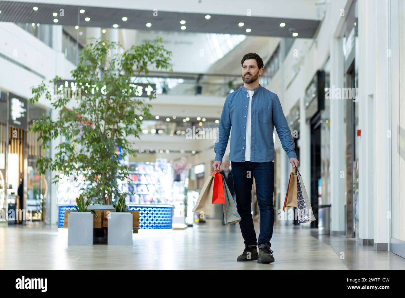 A smiling young man casually dressed walking through a shopping mall ...