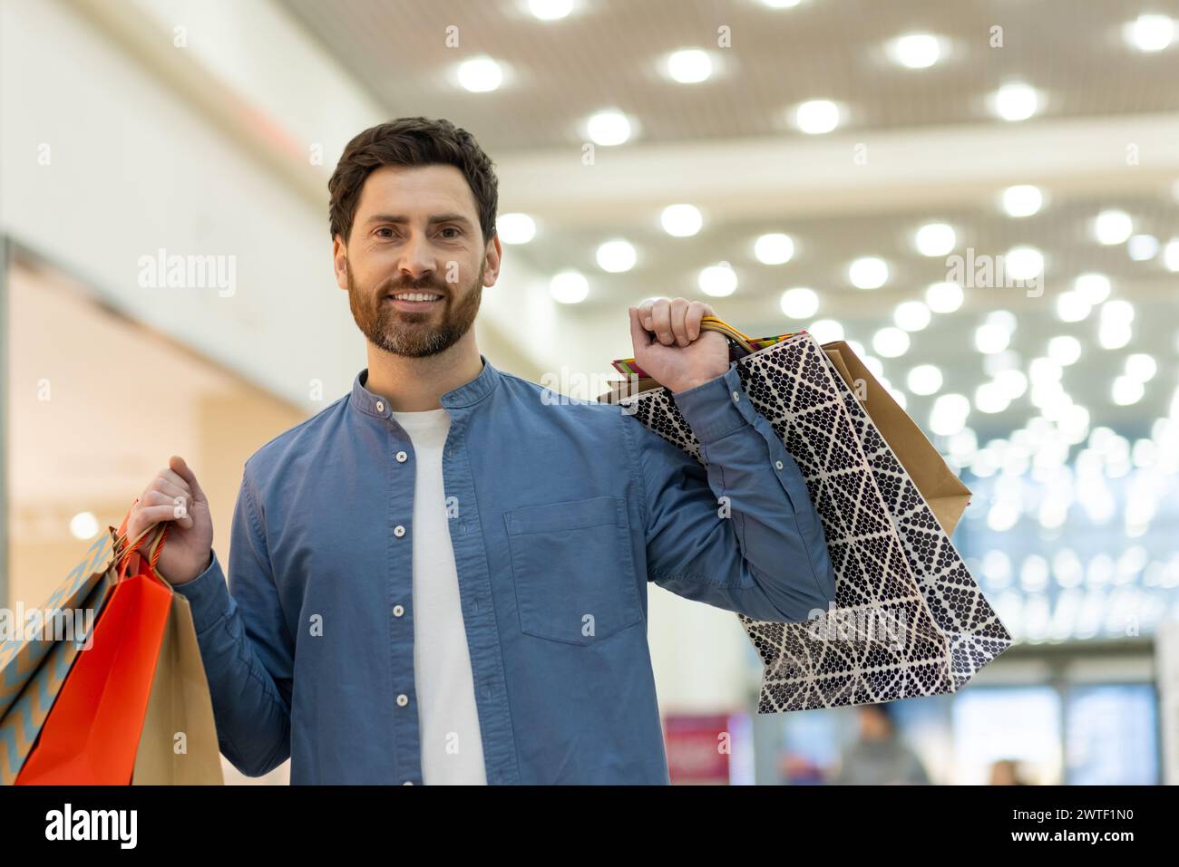 A cheerful man carrying shopping bags, smiling at the camera in a ...