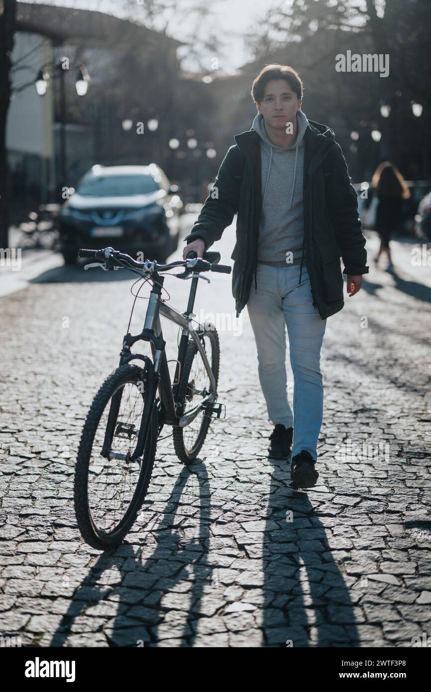 Urban cyclist walking with bicycle on a cobbled street in sunlight ...