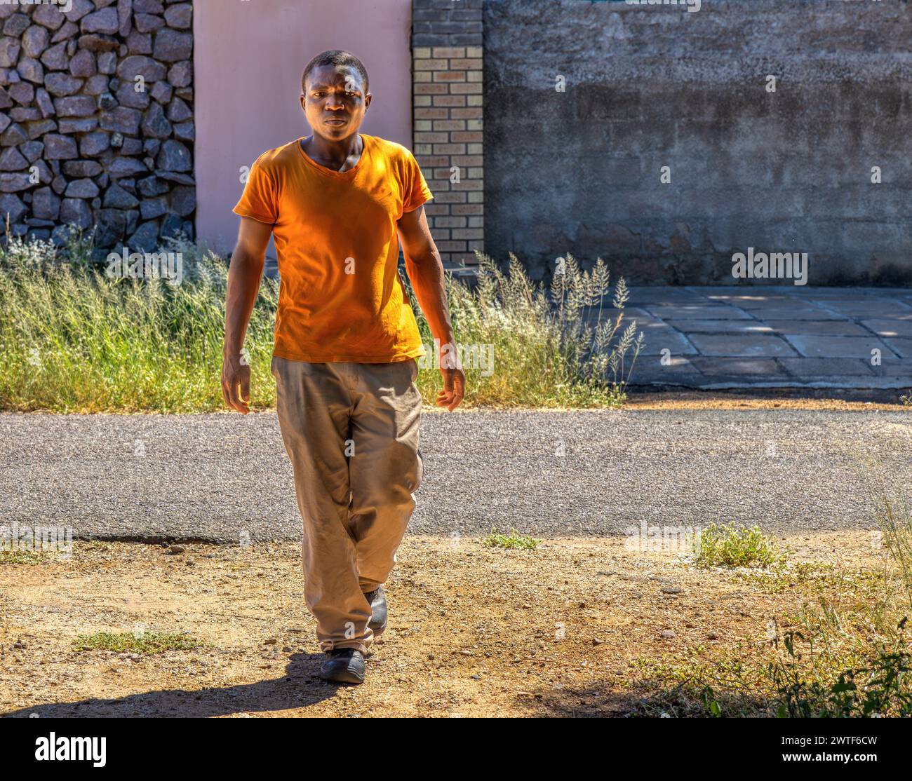 young african man walking in the street, he is wearing an orange t ...