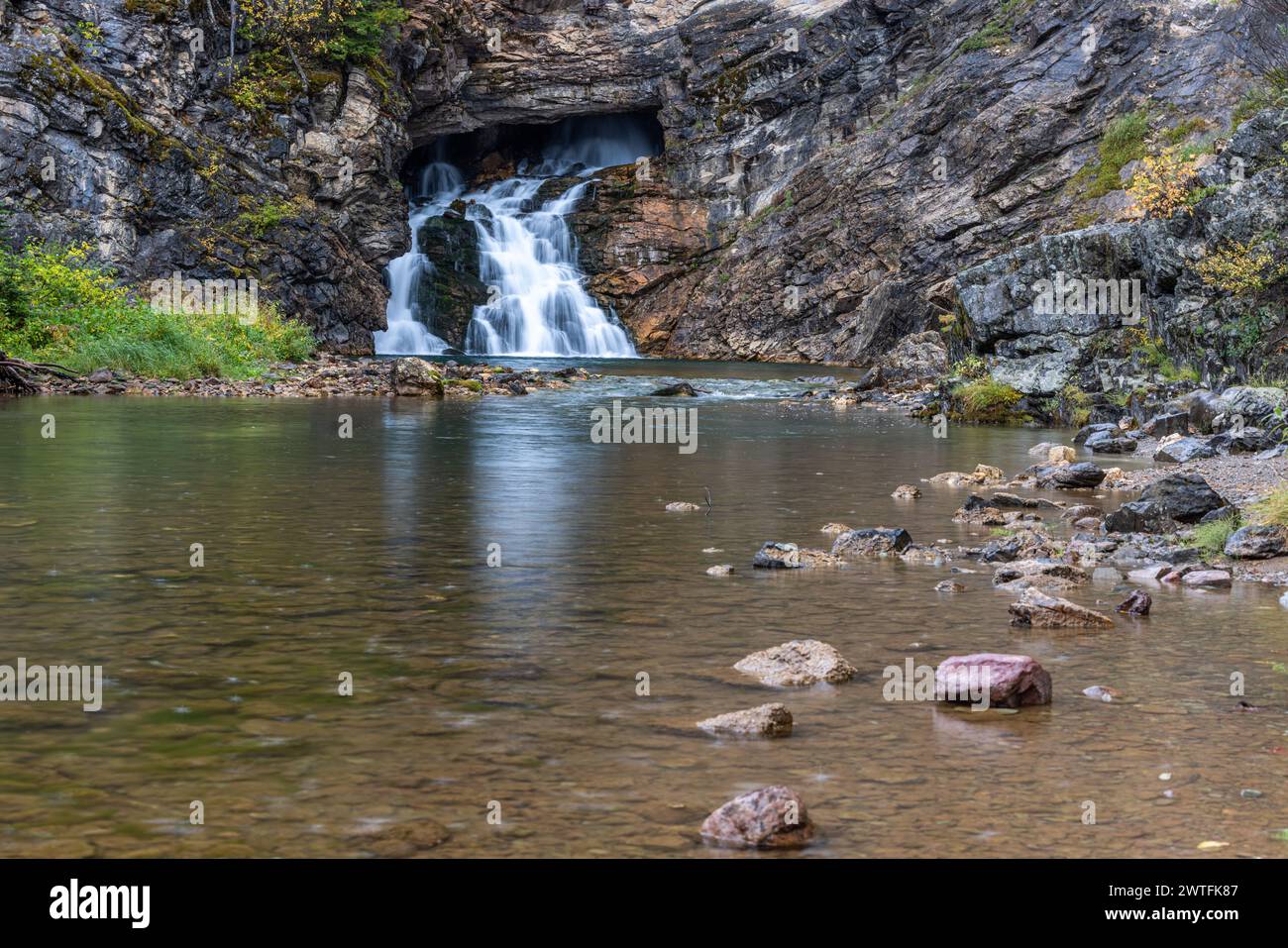 A waterfall is flowing into a river with rocks and pebbles in the water ...