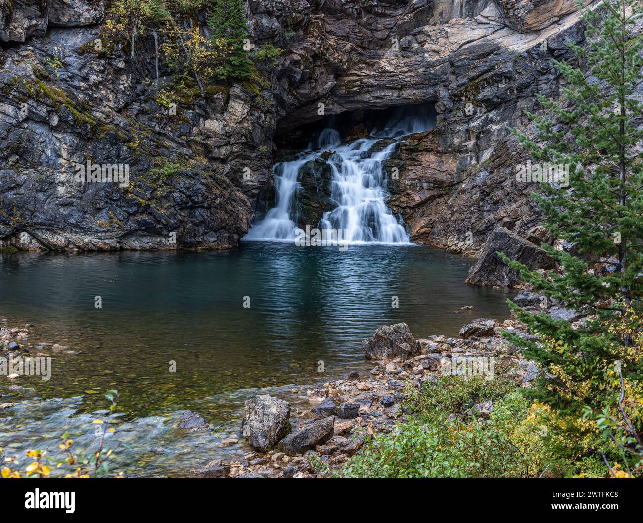 A waterfall is flowing into a small pond. The water is clear and calm ...