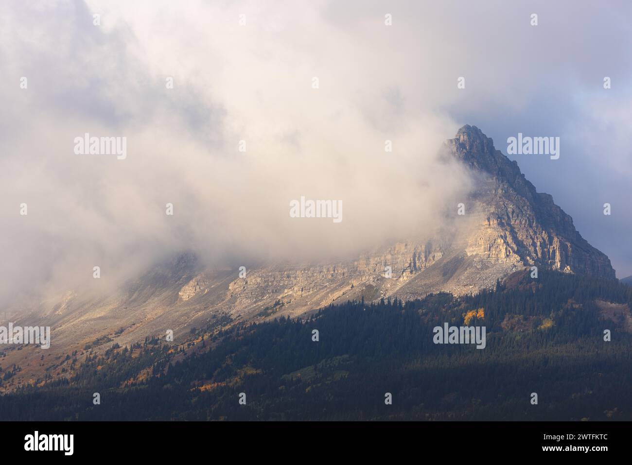 A mountain covered in clouds with a rocky peak. The clouds are white ...