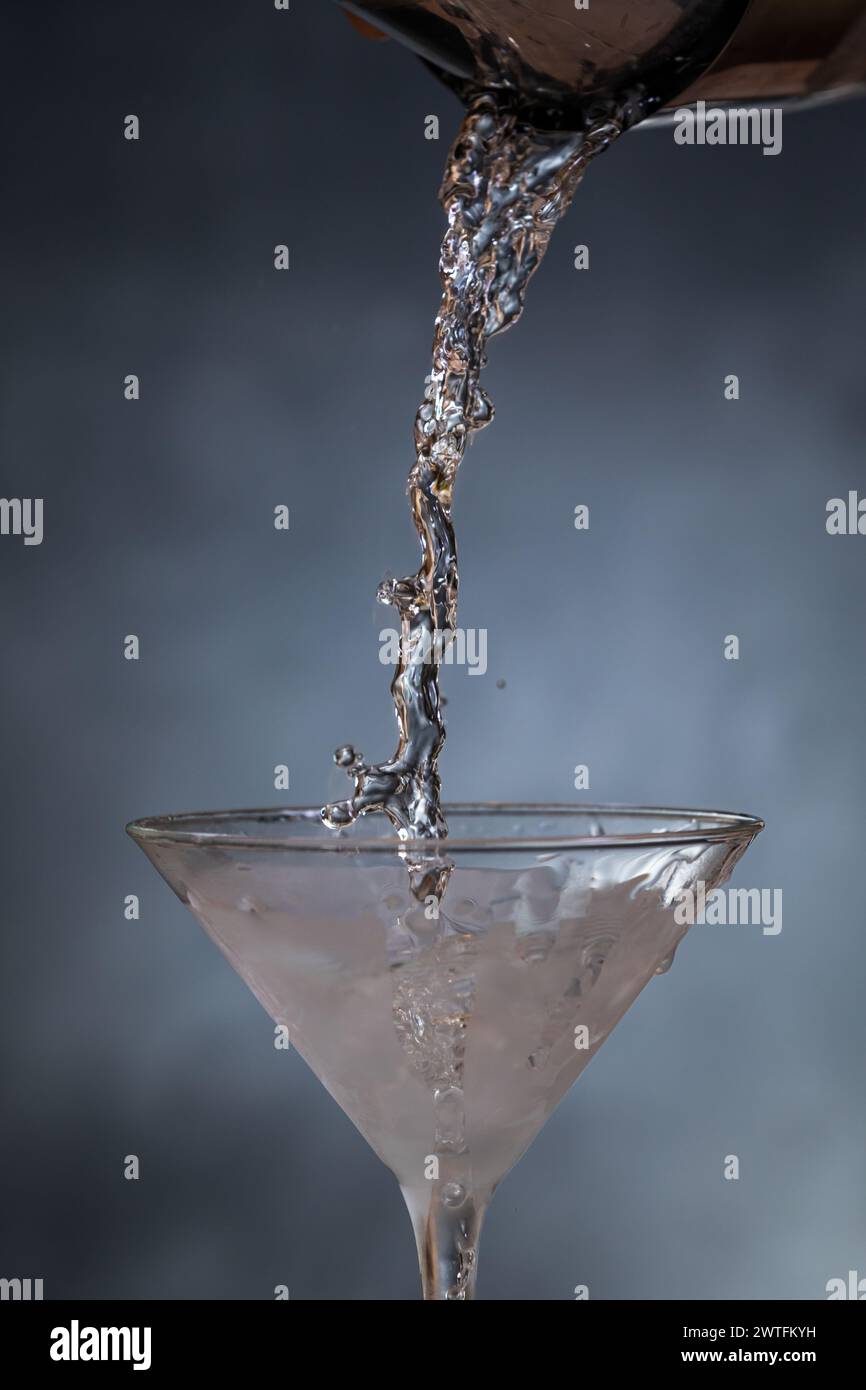 Action shot of pouring chilled gin into a martini glass over a blueish background Stock Photo ...