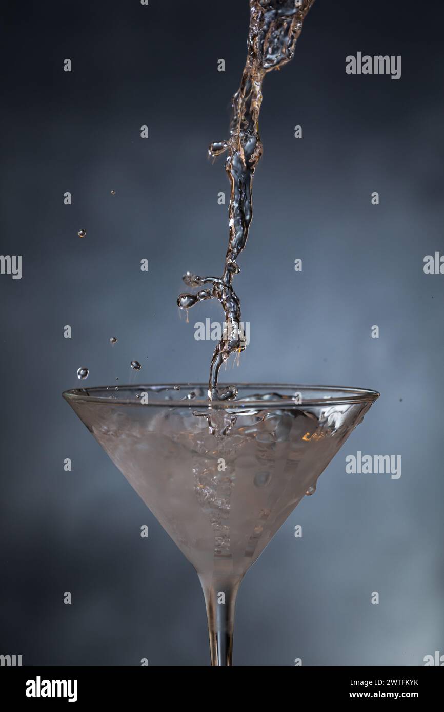 Action shot of pouring chilled rum into a martini glass over a blueish ...