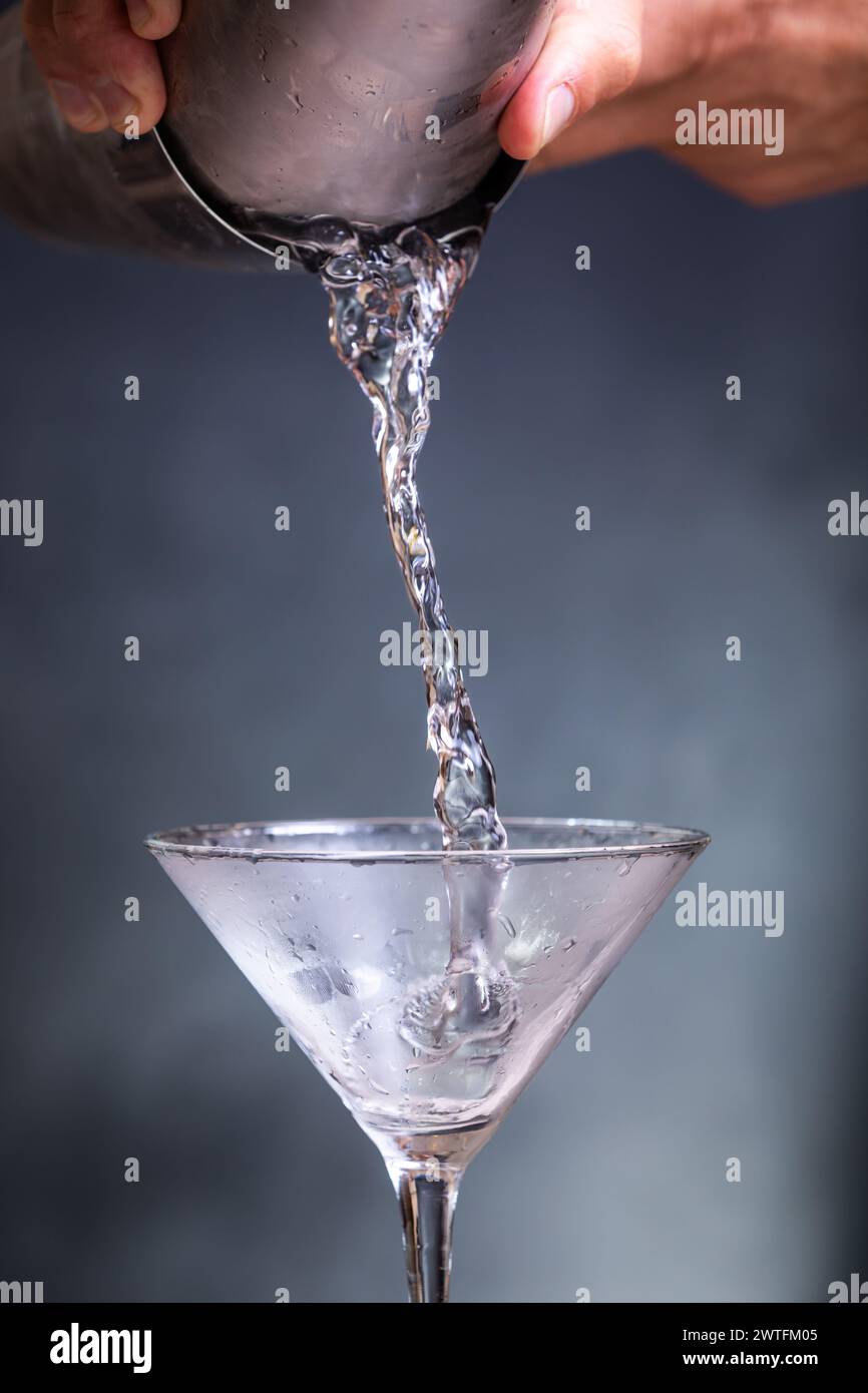 Action shot of pouring chilled gin into a martini glass over a blueish background Stock Photo ...