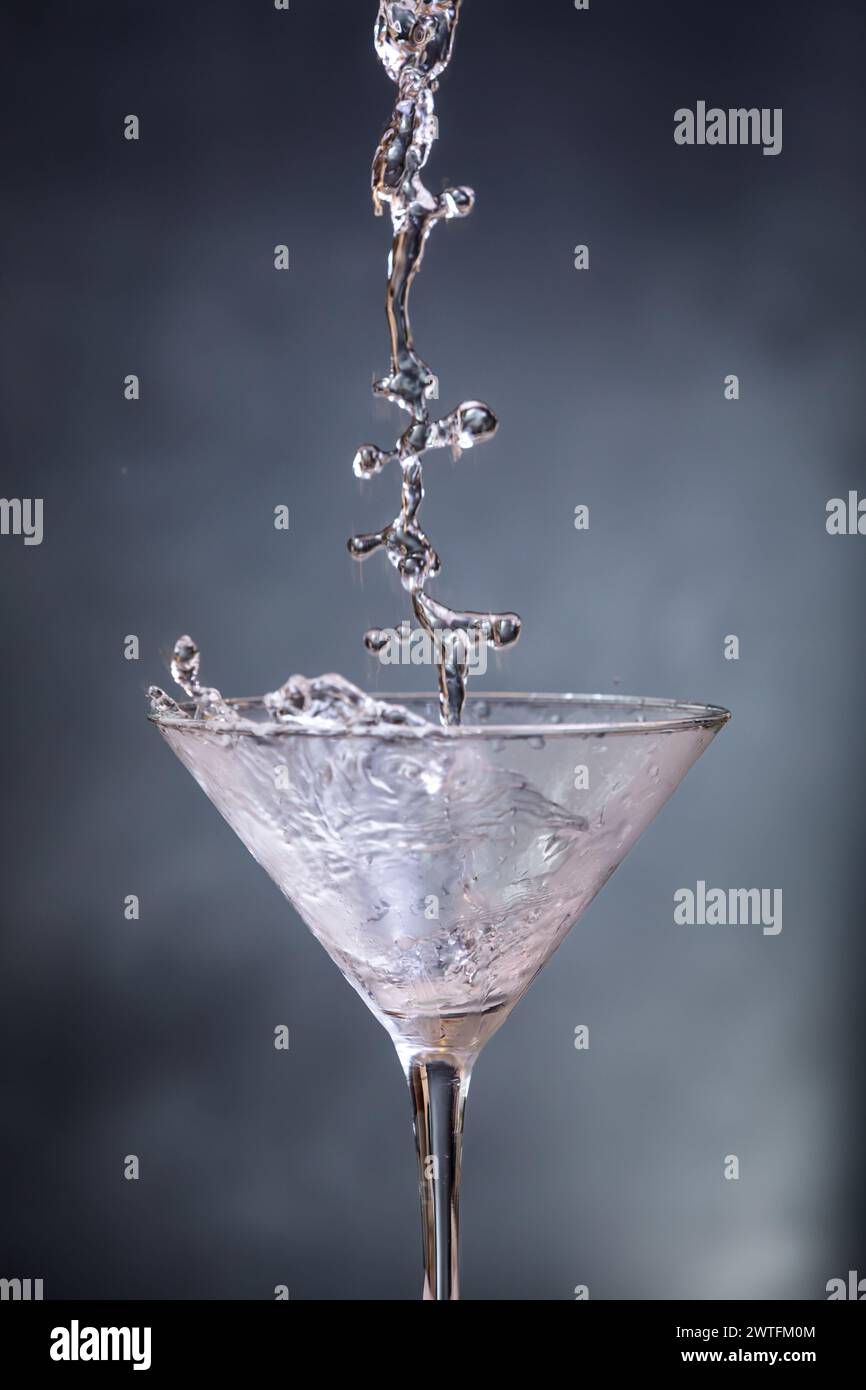 Action shot of pouring chilled gin into a martini glass over a blueish background Stock Photo ...