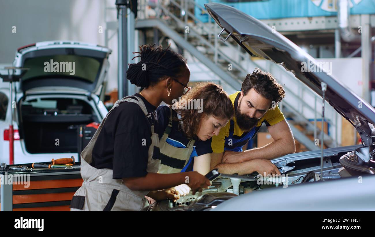 Team of repairmen in car service using inspection lamp to fix busted ...