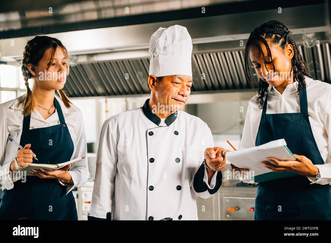 In a restaurant kitchen senior Asian chef educates multiracial students ...