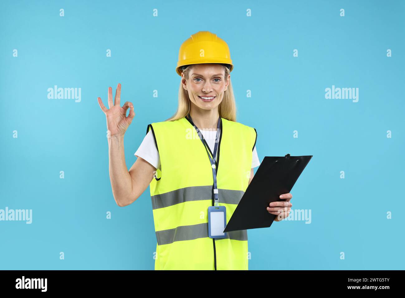 Engineer in hard hat holding clipboard and showing ok gesture on light ...