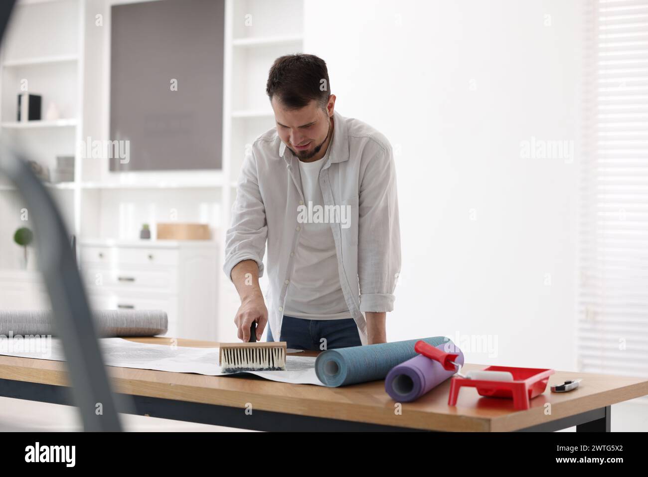 Man applying glue onto wallpaper sheet at wooden table indoors Stock ...