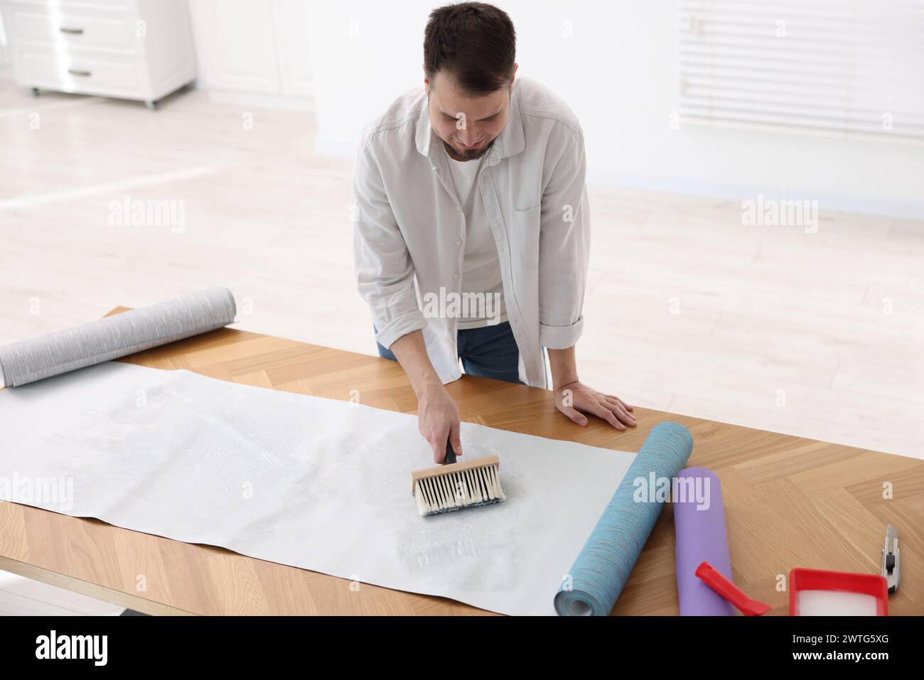 Man applying glue onto wallpaper sheet at wooden table indoors Stock ...