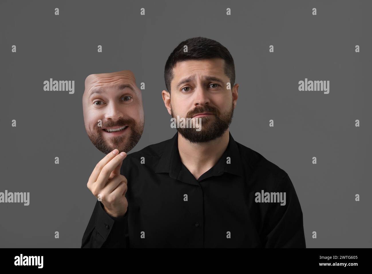 Man holding mask with his facial expression on grey background ...