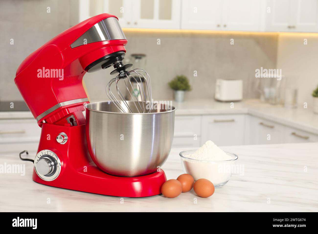 Modern red stand mixer, eggs and bowl with flour on white marble table ...