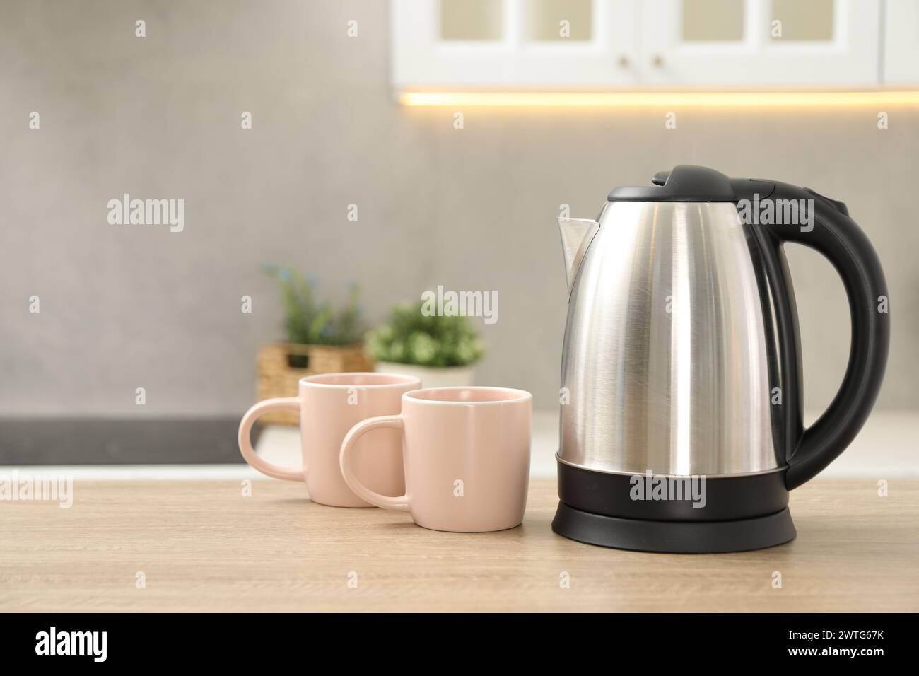 Modern electric kettle and cups on table in kitchen. Space for text ...