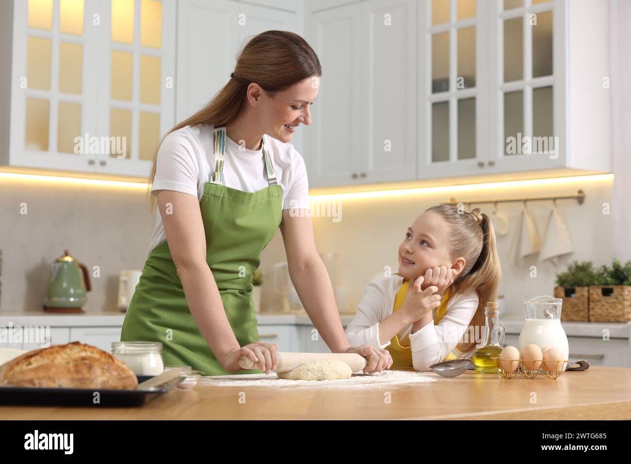 Making bread. Mother and her daughter rolling dough at wooden table in ...
