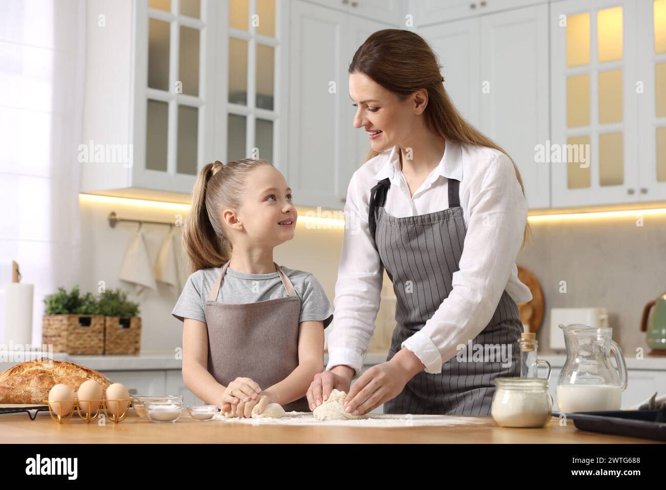 Making bread. Mother and her daughter kneading dough at wooden table in ...