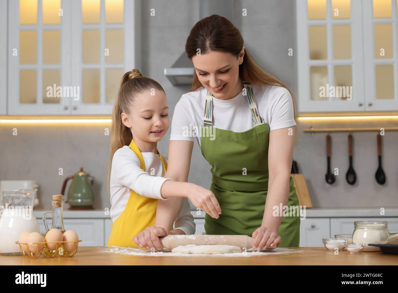 Making bread. Mother and her daughter rolling dough at wooden table in ...