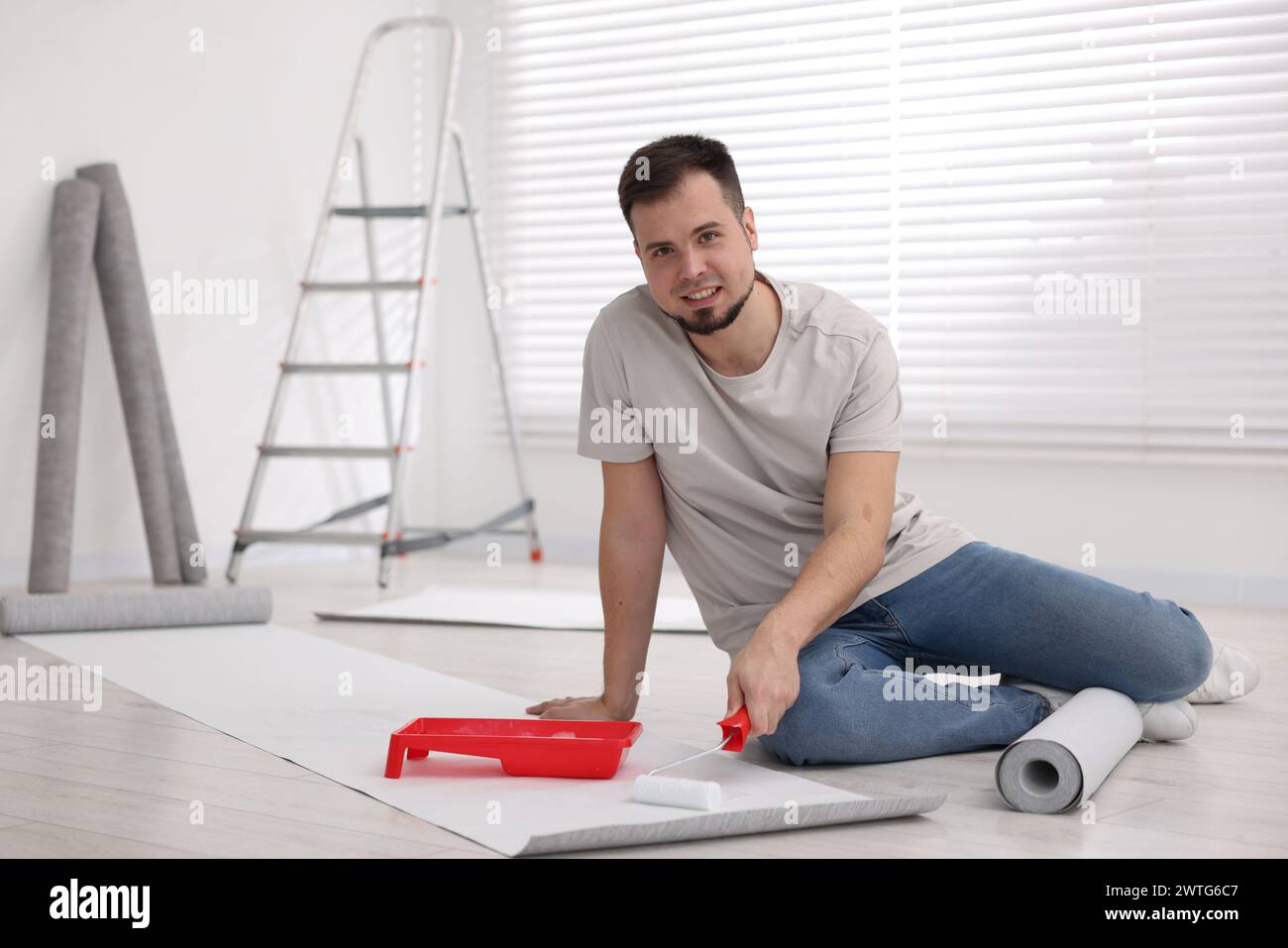 Man applying glue onto wallpaper sheet in room Stock Photo - Alamy