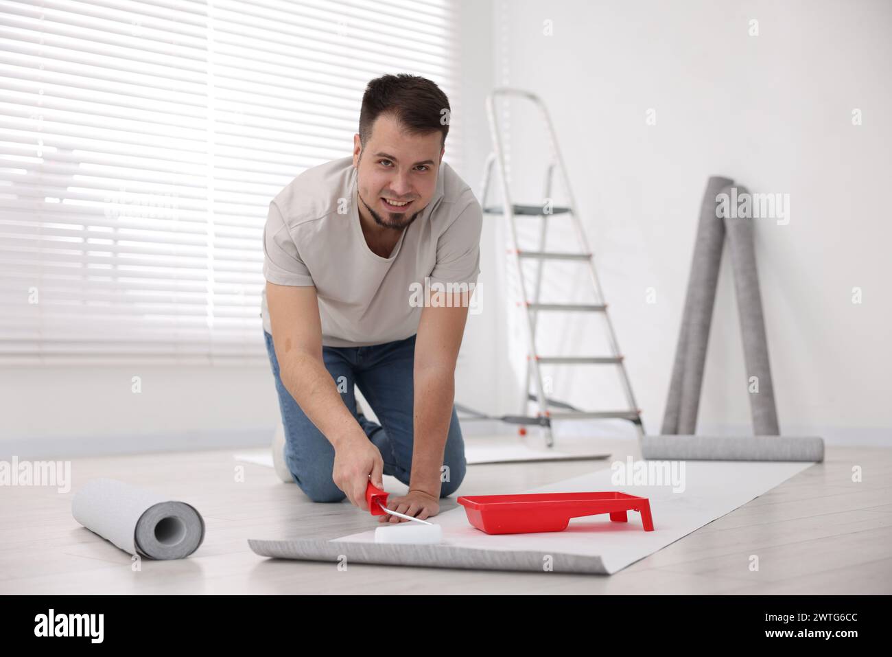 Man applying glue onto wallpaper sheet in room Stock Photo - Alamy