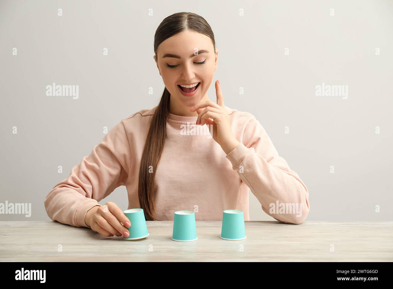 Shell game. Happy woman showing ball under cup at wooden table Stock Photo - Alamy