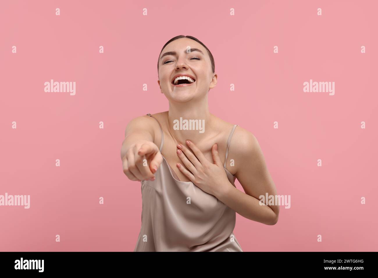 Beautiful woman pointing at something and laughing on pink background ...