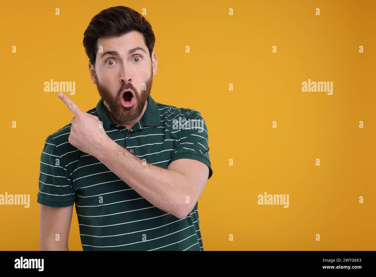 Surprised man pointing at something on yellow background, space for ...
