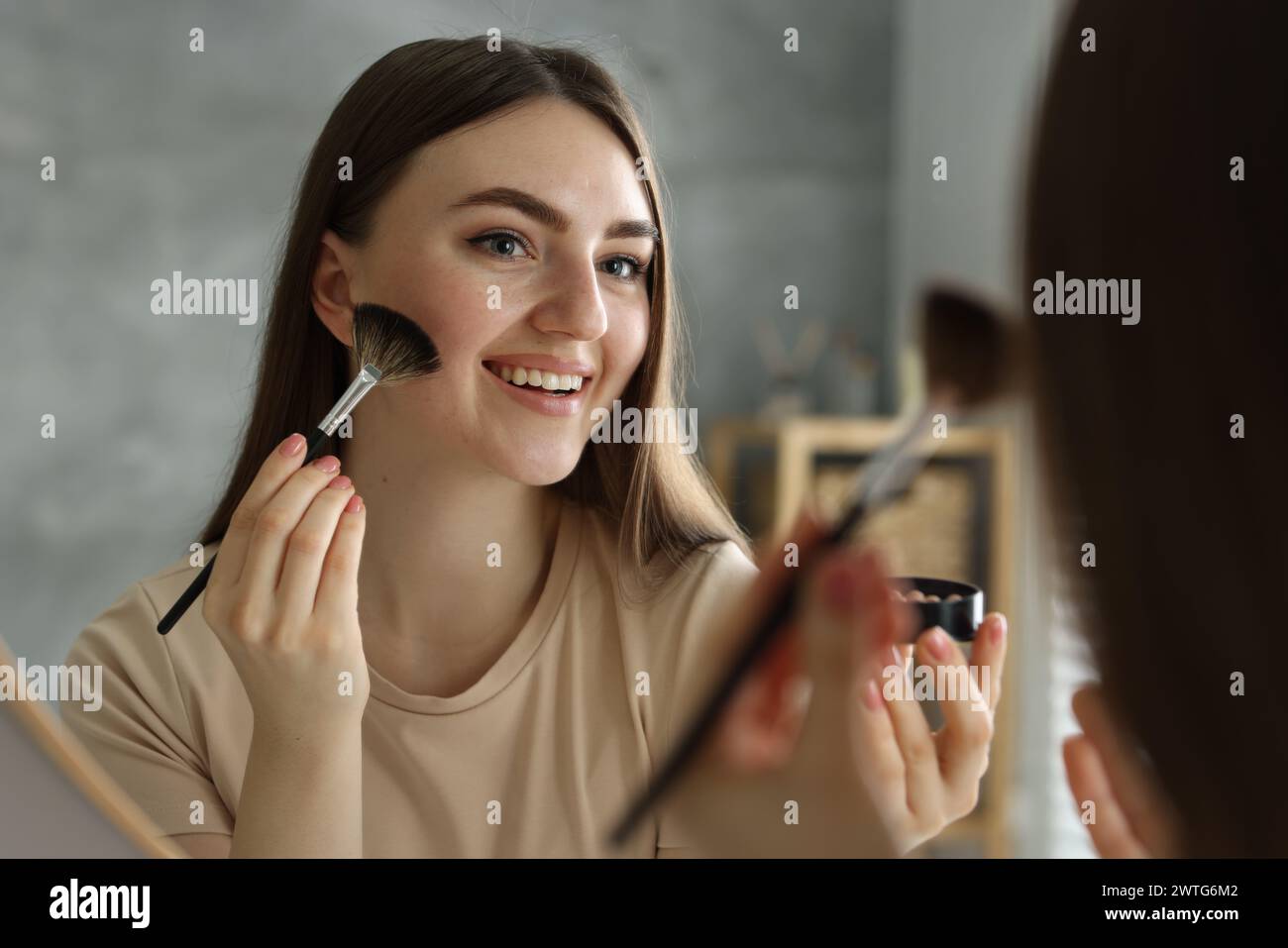 Smiling woman with freckles applying makeup near mirror indoors Stock ...