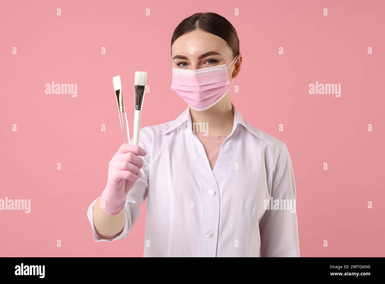 Cosmetologist with cosmetic brushes on pink background Stock Photo - Alamy