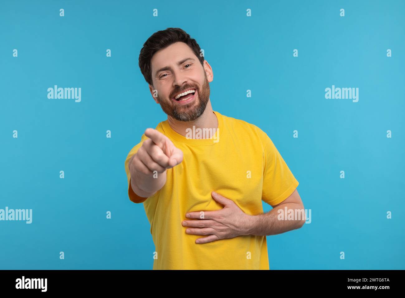 Handsome man pointing at something and laughing on light blue ...