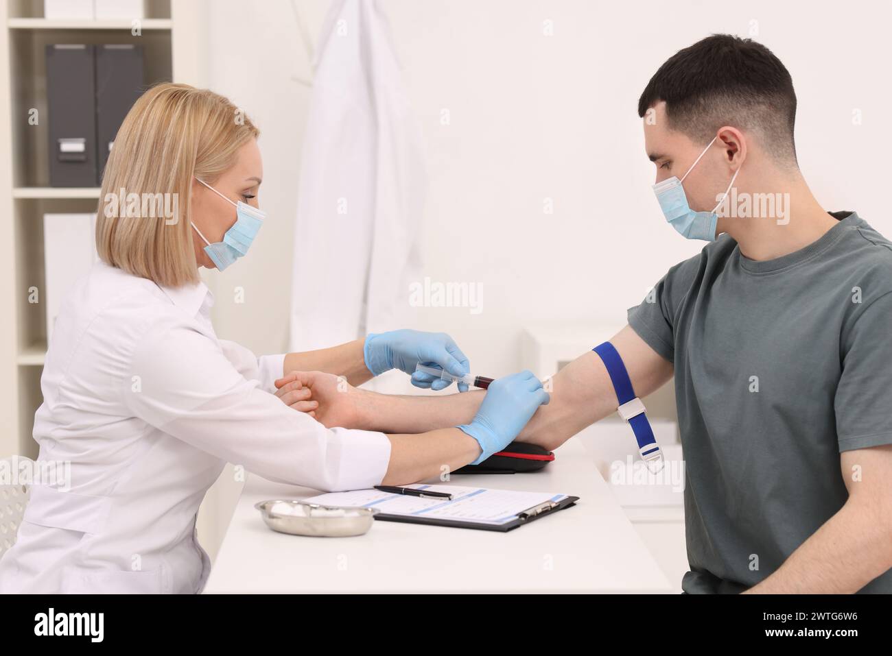 Doctor taking blood sample from patient with syringe at white table in ...