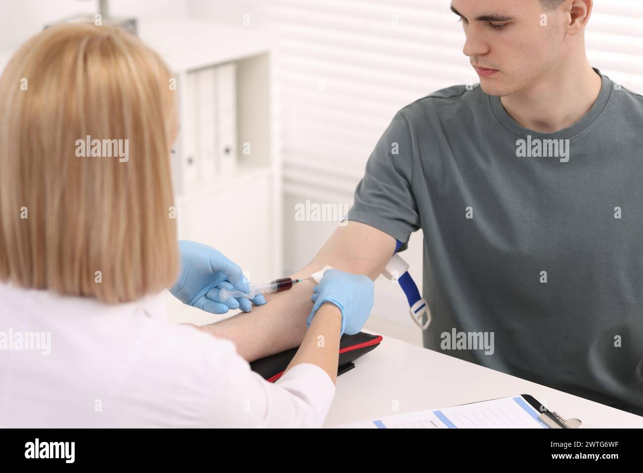 Doctor taking blood sample from patient with syringe at white table in ...
