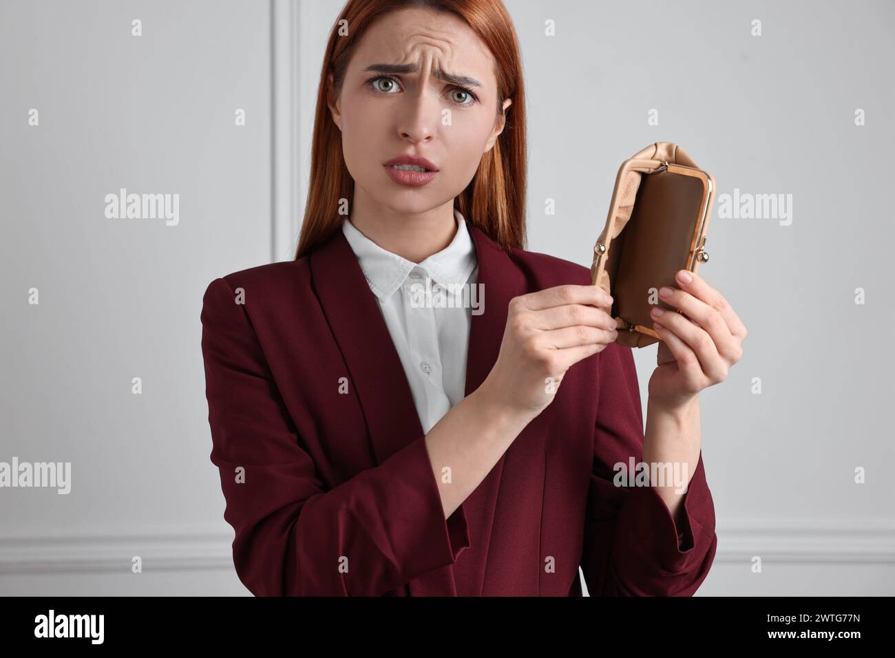 Upset woman with empty wallet near white wall Stock Photo - Alamy