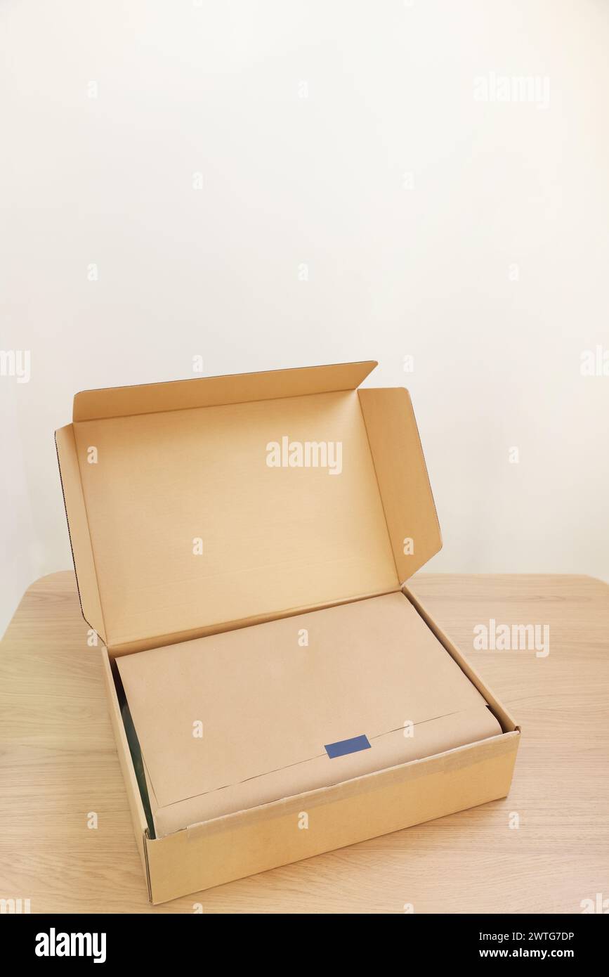 Open cardboard box with item wrapped in kraft paper on wooden table ...