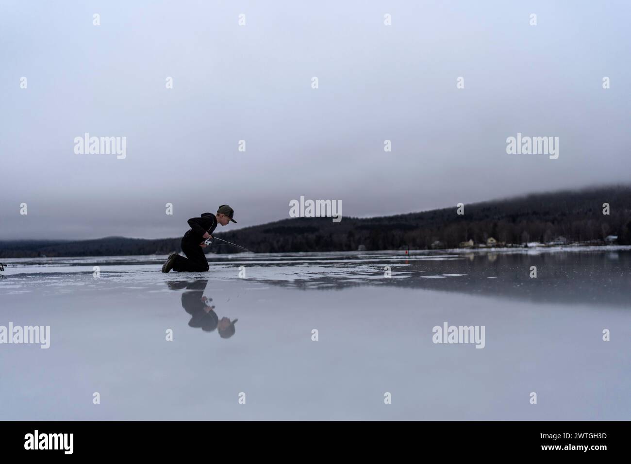 Emmett Adams, 11, looks down into the hole while ice fishing on a ...