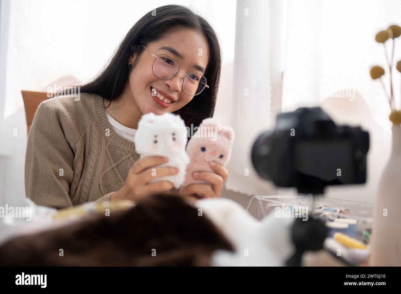 A cheerful young Asian female content creator showing her cute handmade ...