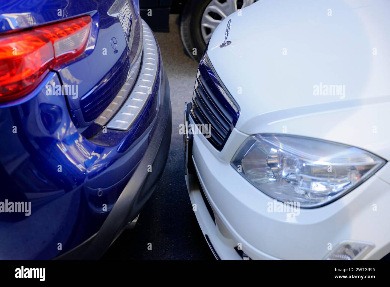 Two cars parked close together, blue car behind, white car in front ...