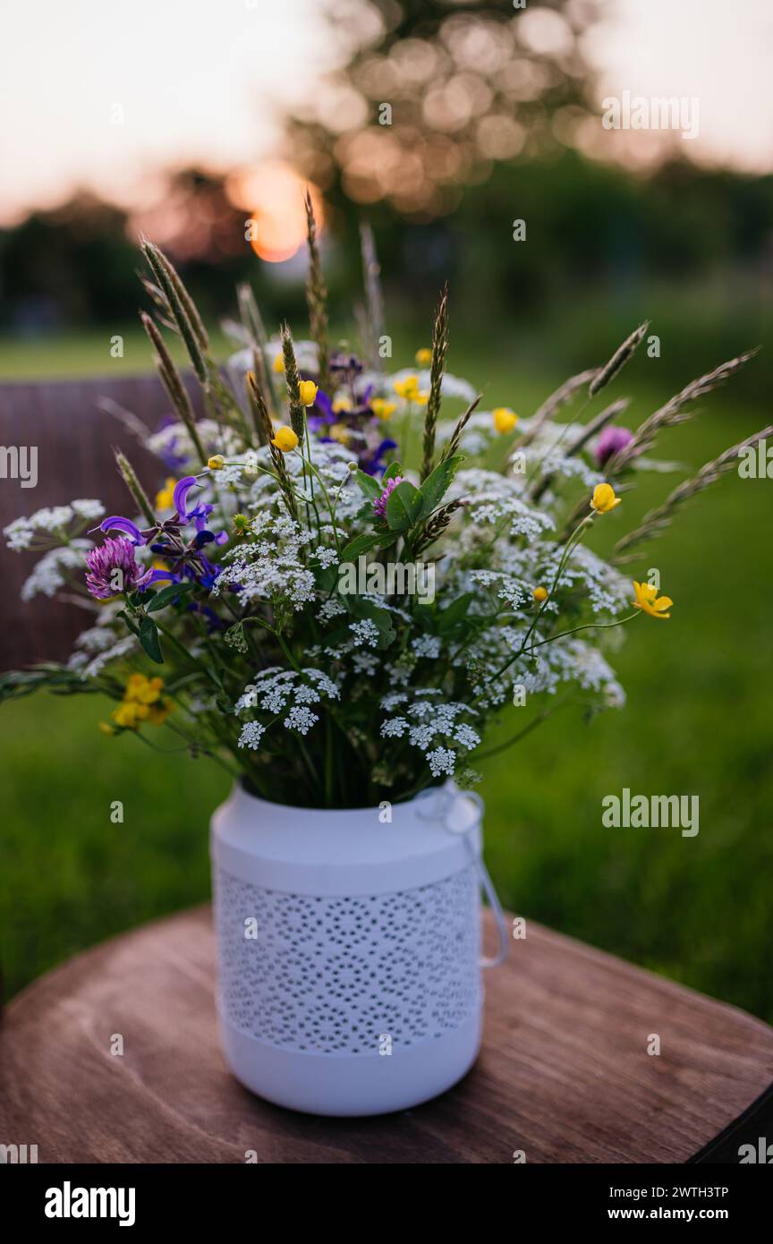 White outdoor vase with meadow flowers, herbs and grass. A colorful ...