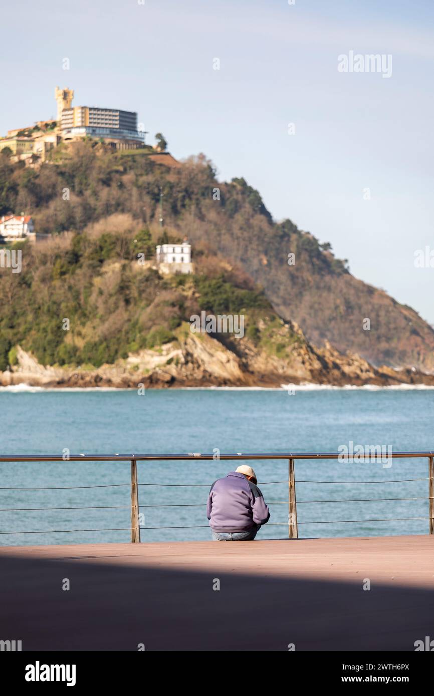 Man sitting down, bent over, against a balustrade near the ocean in San ...