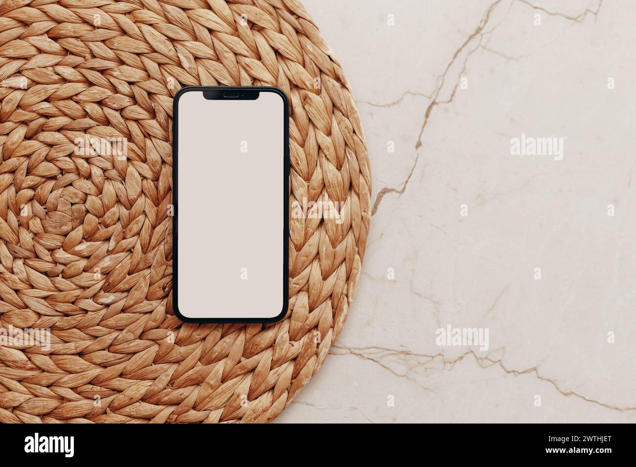 Smartphone with Blank screen on round rattan casket and beige marble ...