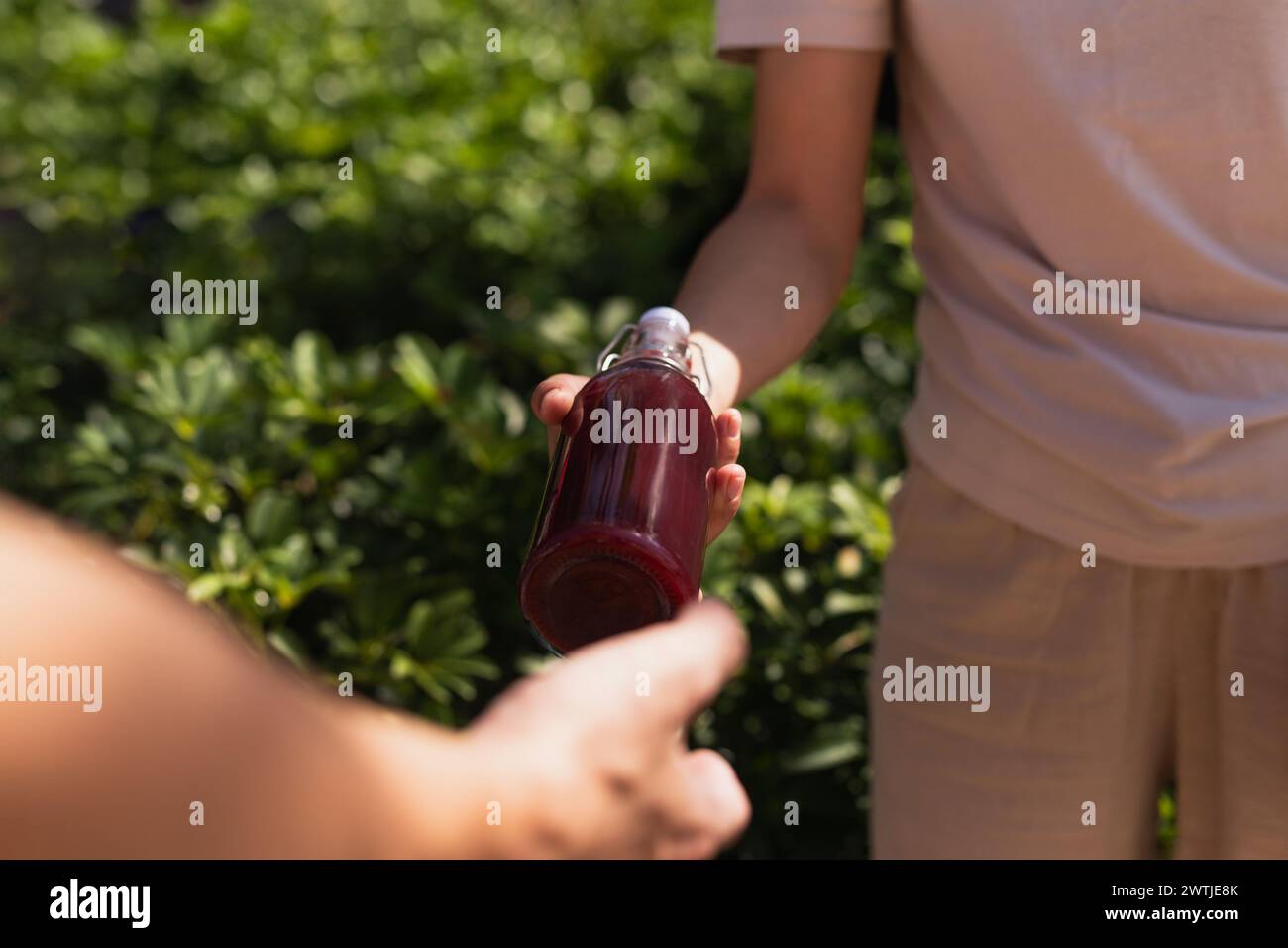 Woman's hand giving a glass bottle of nutritious juice drink with plant ...